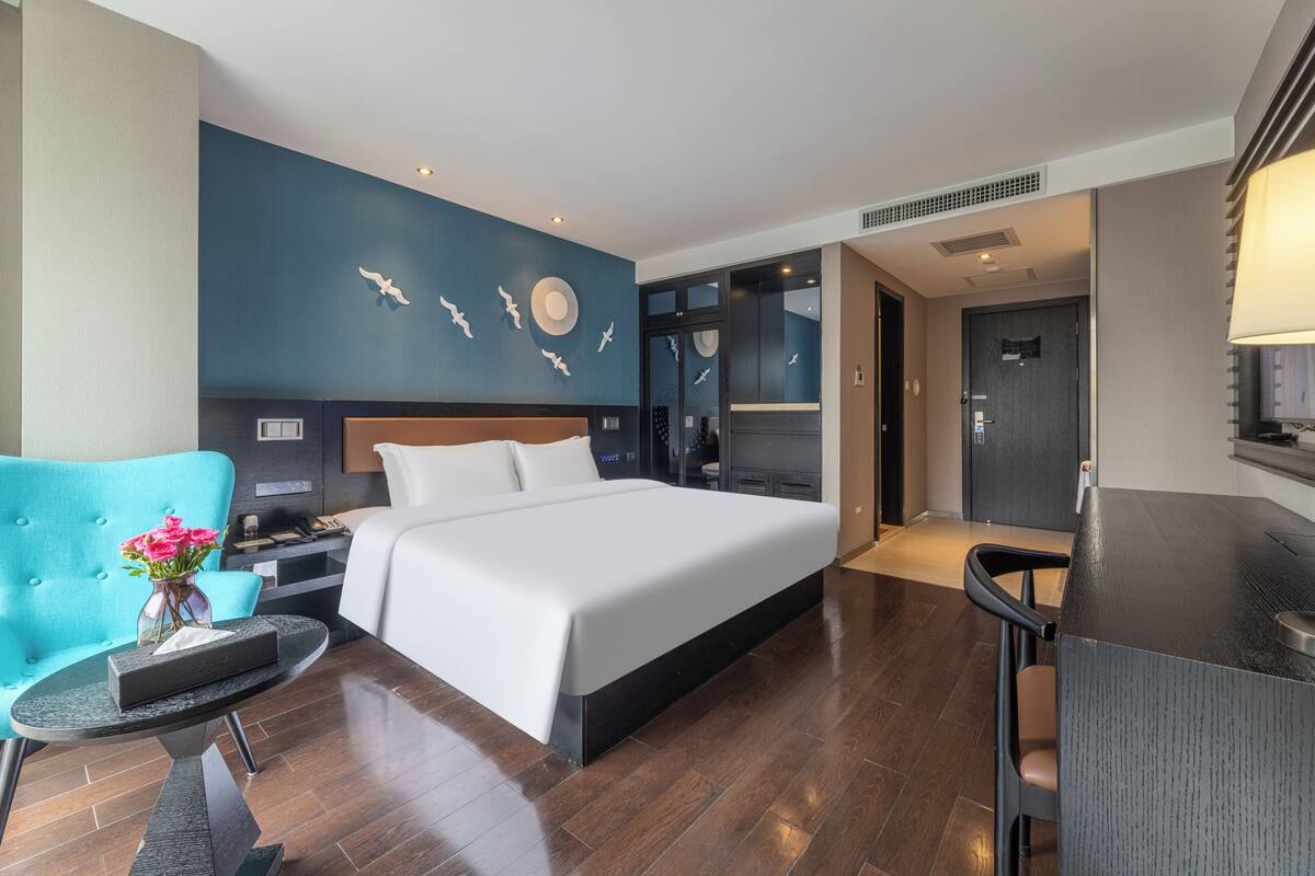 Quarto de hotel moderno com uma cama grande, área de estar com uma mesa, televisão e escrivaninha.