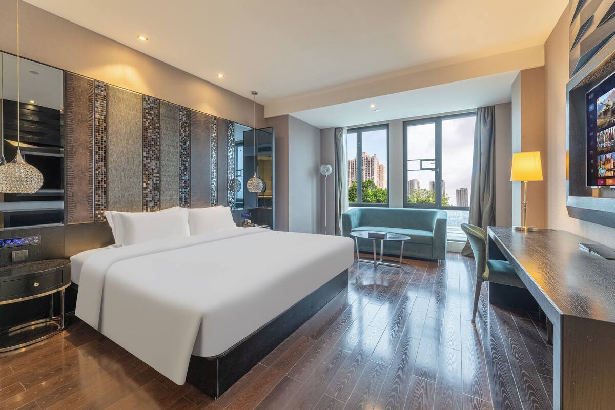 Quarto de hotel moderno com uma cama grande, televisão, escrivaninha e vista para a cidade.