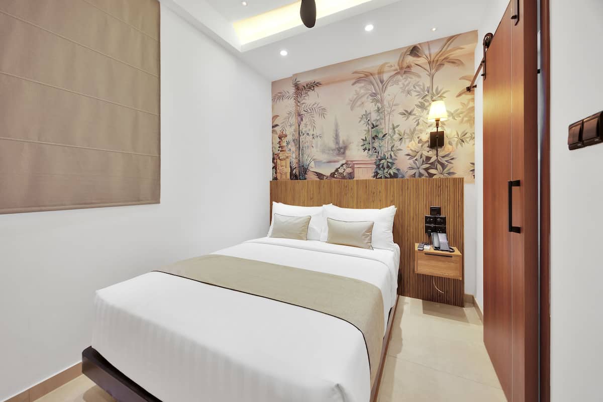 Quarto de hotel com uma cama, uma mesinha de cabeceira com abajur e um mural na parede.