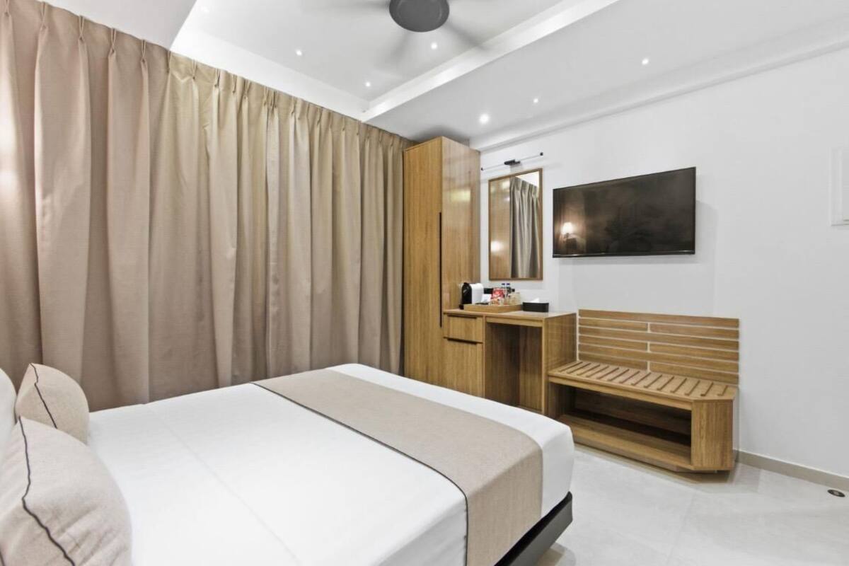 Quarto de hotel moderno com uma cama grande, um banco de madeira, uma escrivaninha e um espelho.