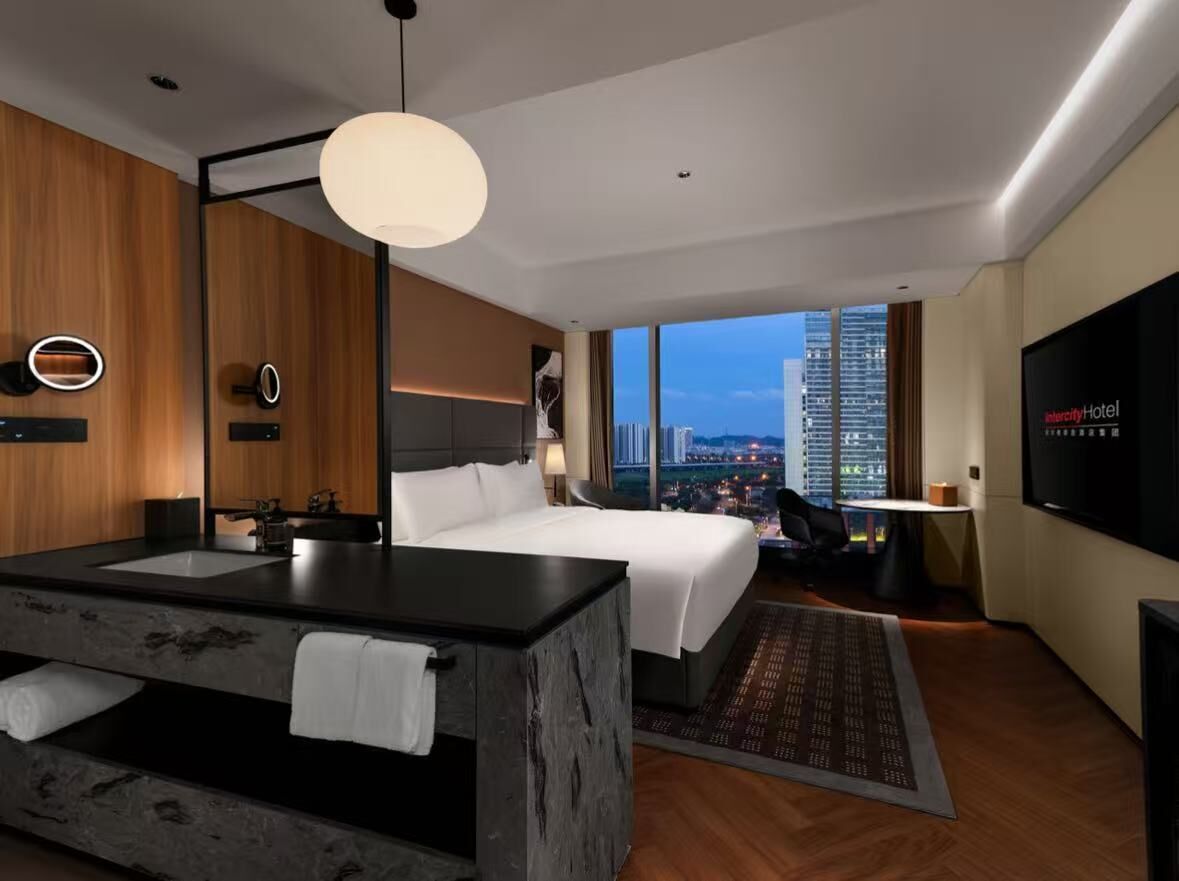 Quarto de hotel moderno com uma cama grande, banheiro com toucador de mármore, vista para a cidade e televisão de tela plana.