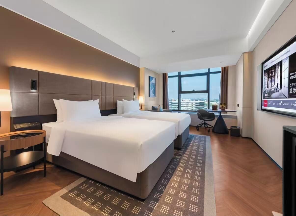Quarto de hotel com cama grande, escrivaninha, cadeira, televisão e vista para a cidade.