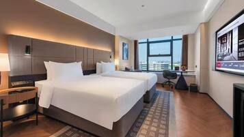 Quarto de hotel com cama grande, escrivaninha, cadeira, televisão e vista para a cidade.