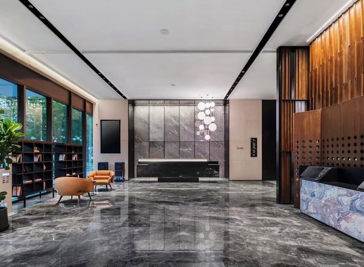 Um lobby moderno com piso de mármore, área de estar, painéis de madeira e um grande luminário fixado na parede.