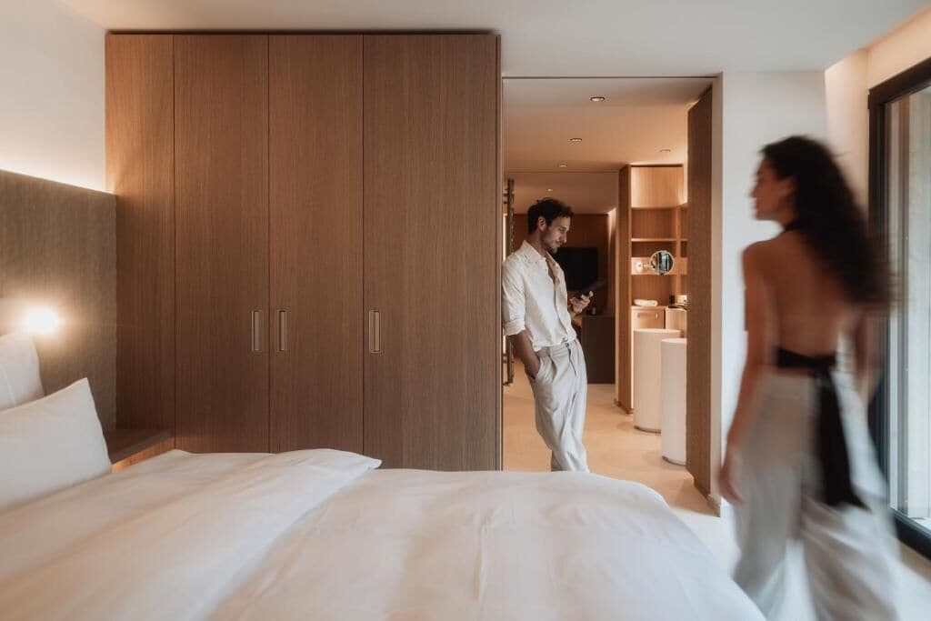Quarto com cama grande, guarda-roupa de madeira e banheiro visível por uma porta aberta.