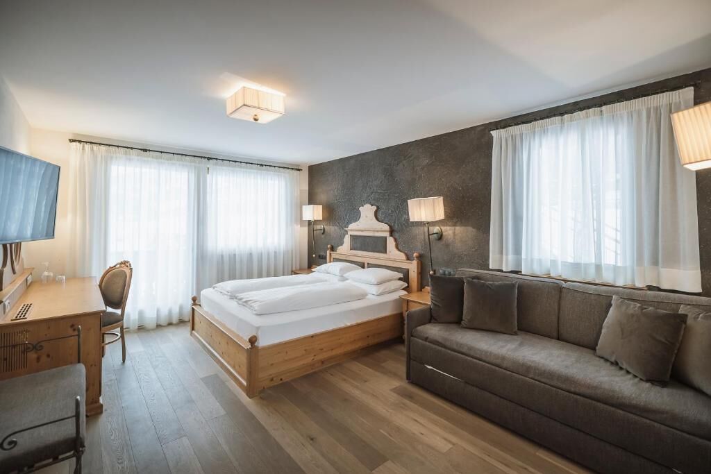 Quarto de hotel com cama, escrivaninha, poltrona, sofá e duas luminárias.