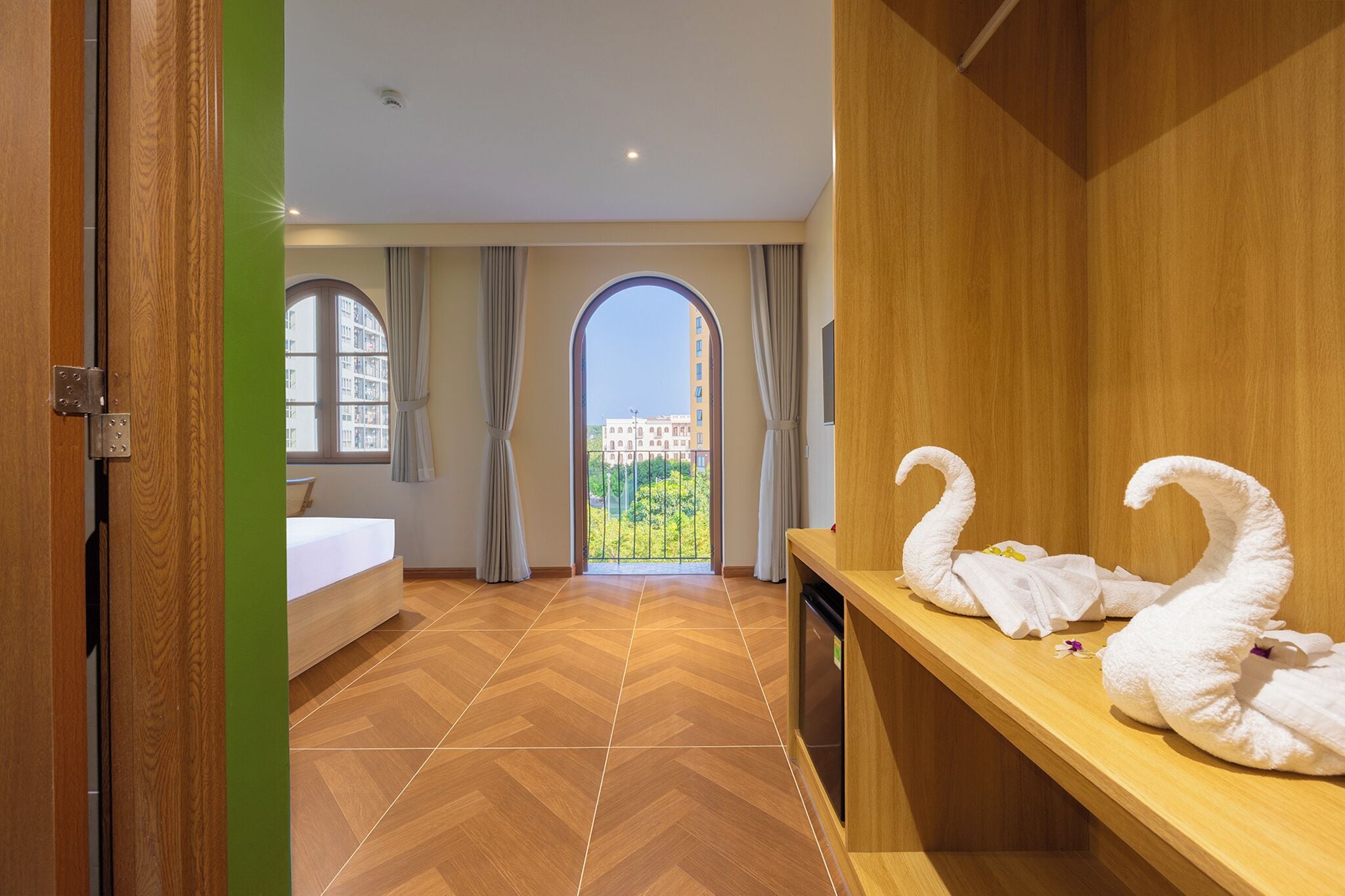 Quarto de hotel com cama, secretária de madeira e toalhas, e vista pela janela.