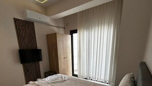 Quarto de hotel com uma cama grande, televisão de tela plana na parede, armário de madeira e janela com cortinas.