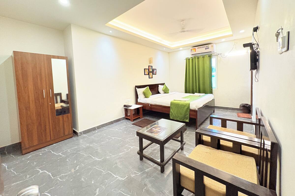 Quarto de hotel com cama, escrivaninha, cadeira, guarda-roupa e ventoinha no teto.