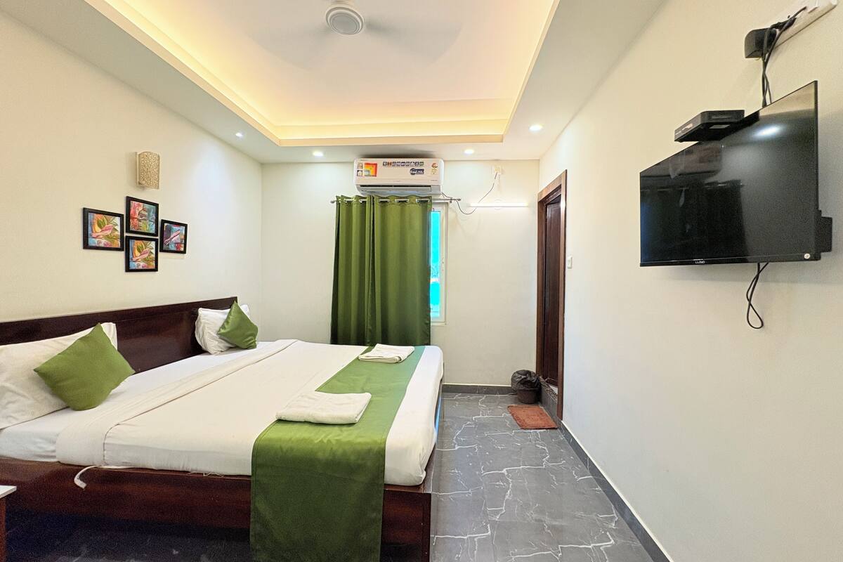 Quarto de hotel com cama, televisão de tela plana na parede, ventoinha no teto e janela com cortinas.