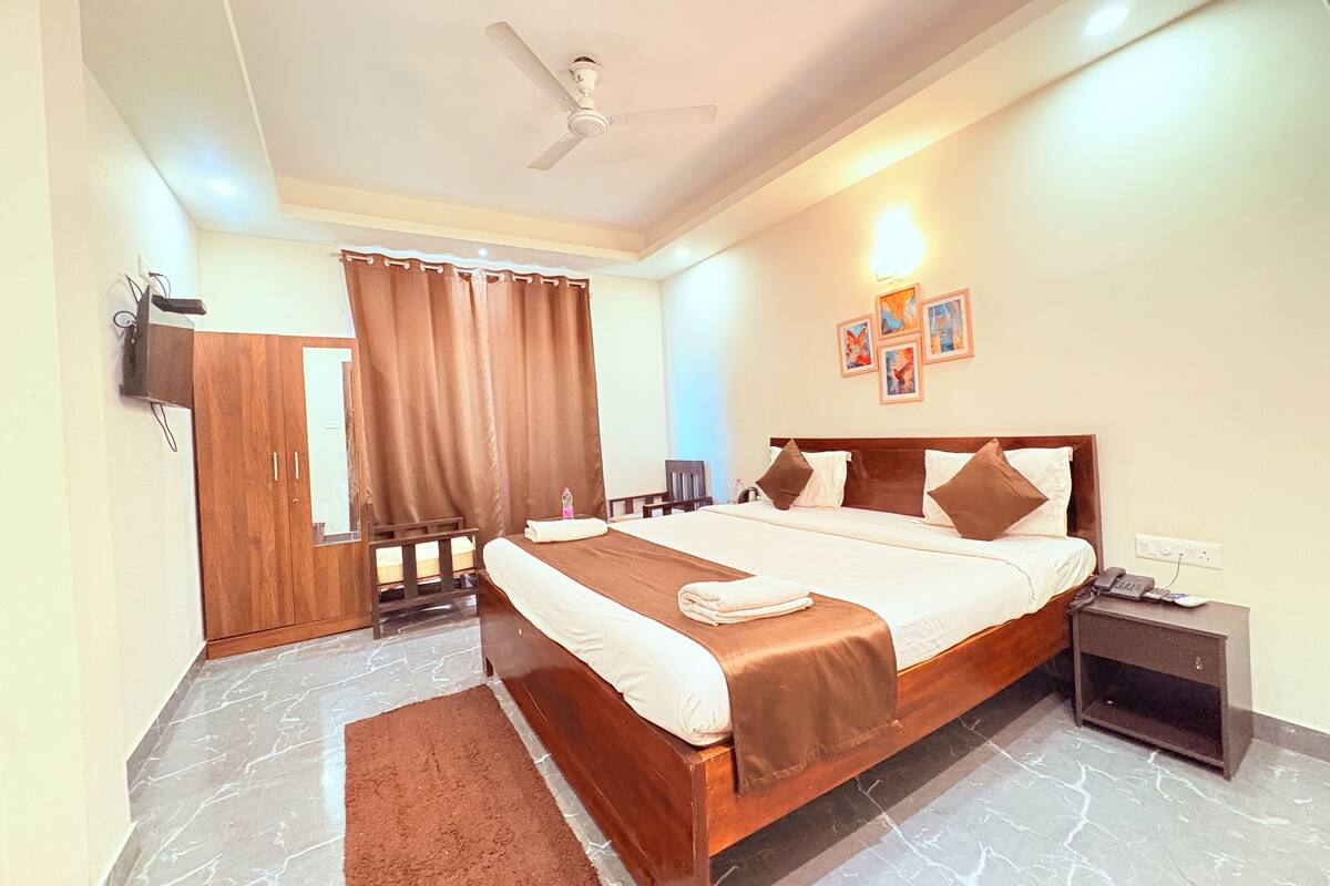 Quarto de hotel com uma cama, ventoinha no teto, mesa de cabeceira, escrivaninha, guarda-roupa e banheiro.
