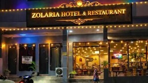 Um hotel com uma placa que diz 'Zolaria Hotel & Restaurant' e uma entrada bem iluminada.