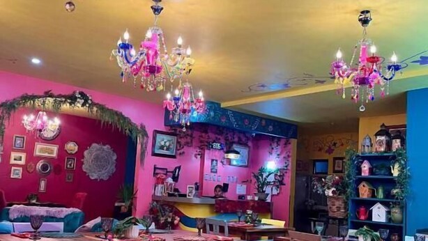 Uma área de refeições vibrante com várias mesas, cadeiras e lustres coloridos.