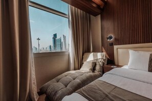 Quarto de hotel com cama, mesa de cabeceira, luminária e vista para o horizonte da cidade pela janela.