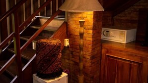Uma escadaria com guarda-corpos de madeira, um abajur com cúpula bege, um objeto estampado sobre um pedestal branco e uma parede de tijolos.