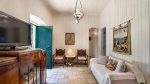 Um quarto com televisão, um armário de madeira, um sofá, uma mesinha com cadeiras e um quadro na parede.