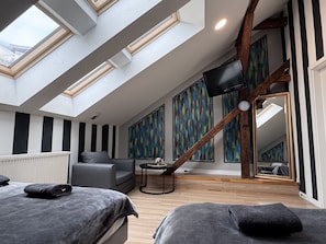 Quarto estilo loft moderno com janelas do teto, televisão, sofá e arte abstrata nas paredes.