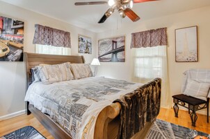 Quarto com cama, uma cadeira, ventoinha no teto e obras de arte nas paredes.