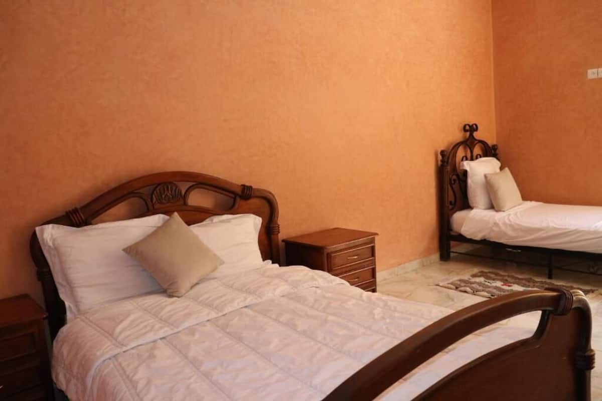 Quarto com cama de madeira, mesa de cabeceira e outra cama ao fundo.