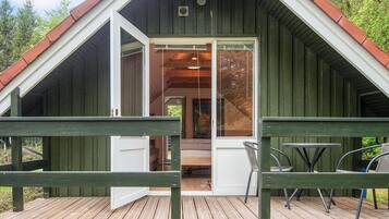 Uma cabana de madeira com telhado inclinado, um deck de madeira e uma porta de vidro que dá para o interior.