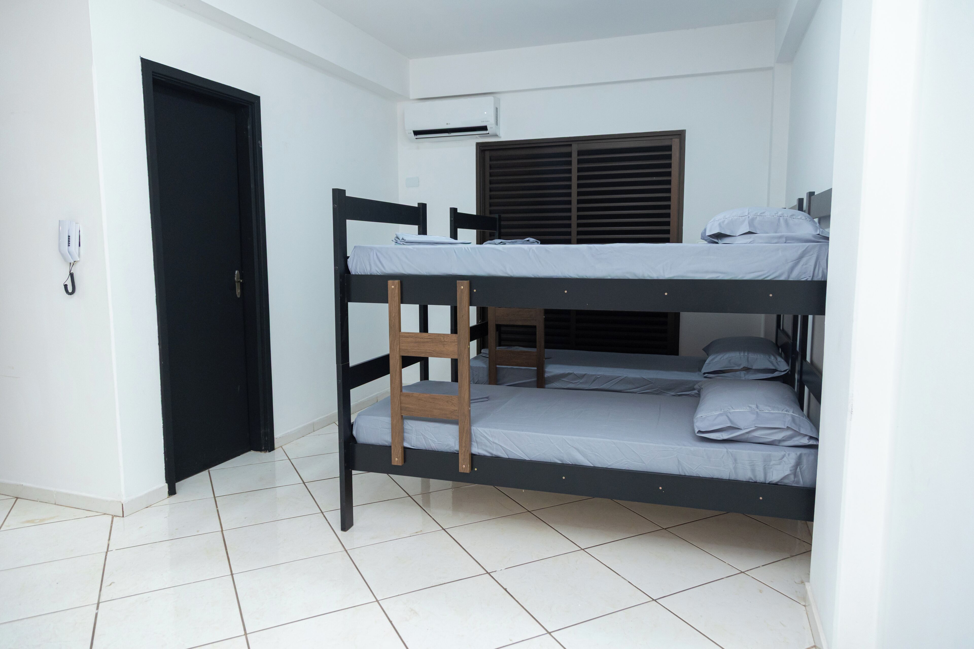 Quarto com beliche, porta, ar condicionado e janela com cortinas.