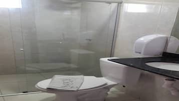 Casa de banho com sanita, cabine de duche e lavatório com dispensador de sabão.