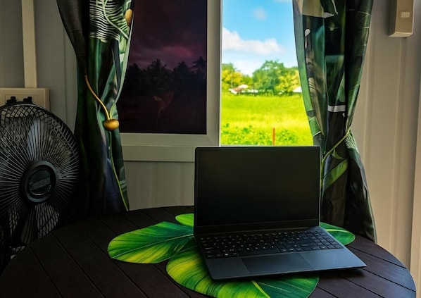 Um laptop sobre uma mesa, com vista para um campo verde pela janela.