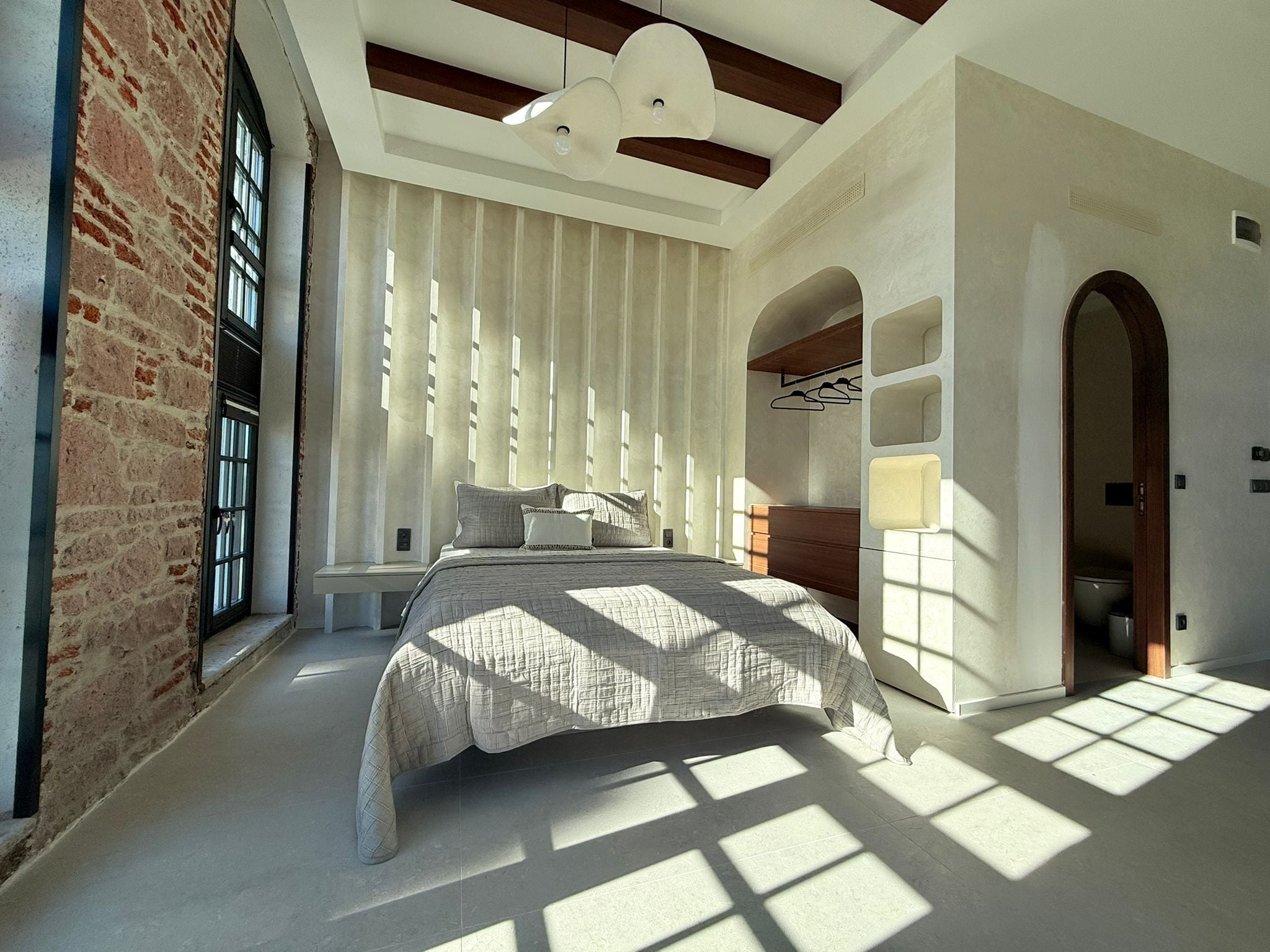 Quarto com uma cama grande, parede de tijolos e claraboia.