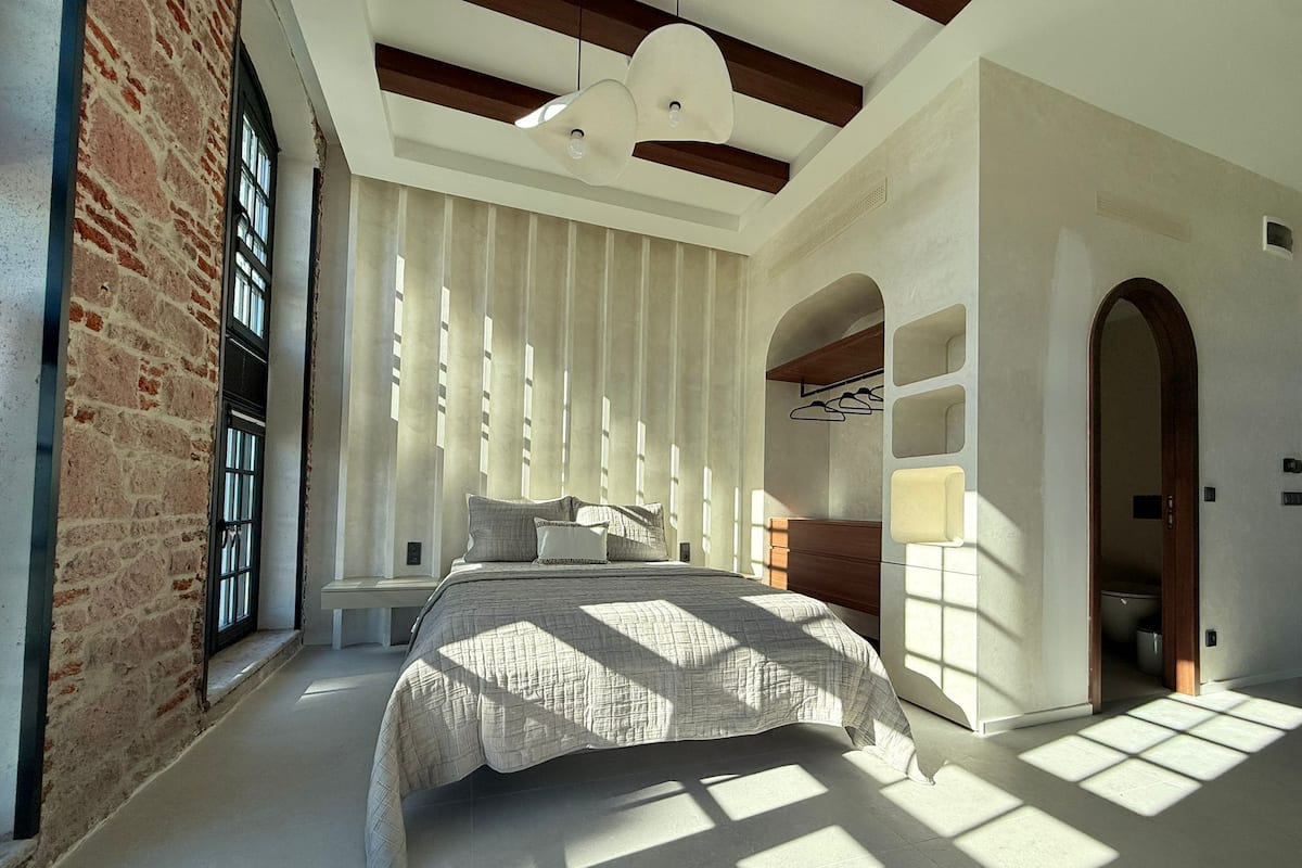 Quarto com uma cama grande, parede de tijolos e claraboia.
