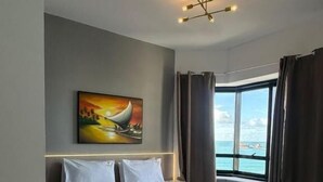 Quarto de hotel com cama, um quadro, janela com cortinas e luminária no teto.