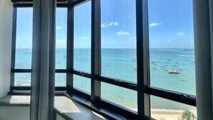 Quarto com amplas janelas com vista para uma praia e o oceano.