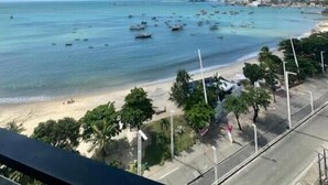 Vista costeira com barcos, uma praia e um horizonte urbano distante.