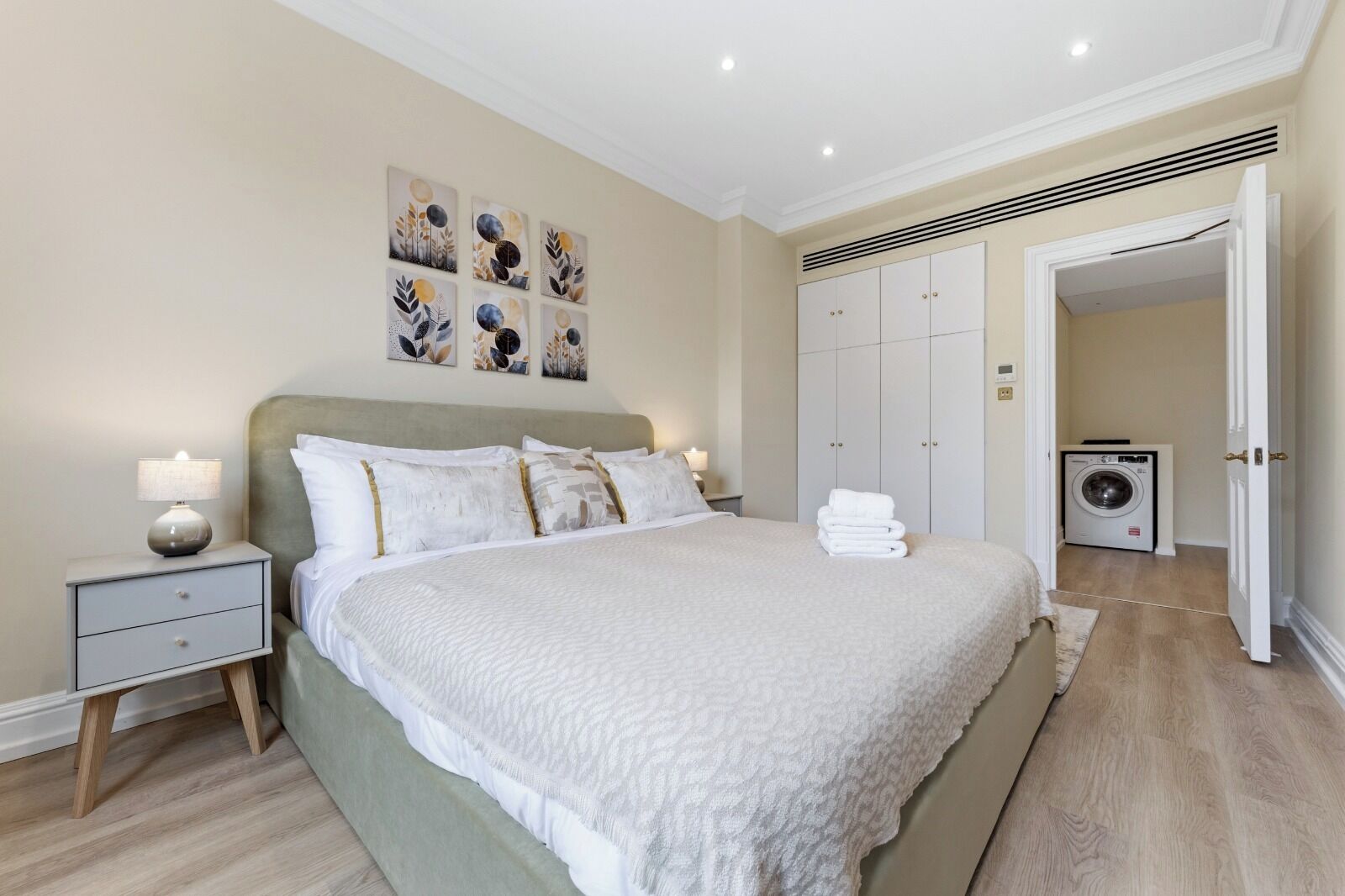 Quarto com cama, mesas de cabeceira, guarda-roupa e máquina de lavar roupa.