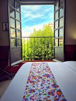 Quarto com cama, janela com vista aberta para uma varanda e colcha colorida.