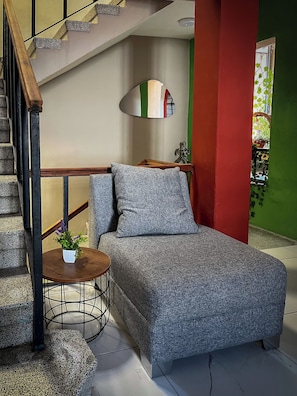 Quarto com uma cama, uma mesinha com uma planta, um espelho e uma escada.