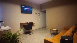 Uma sala de estar moderna com televisão de tela plana, uma mesa de centro de madeira, sofá, escrivaninha e planta em vaso.