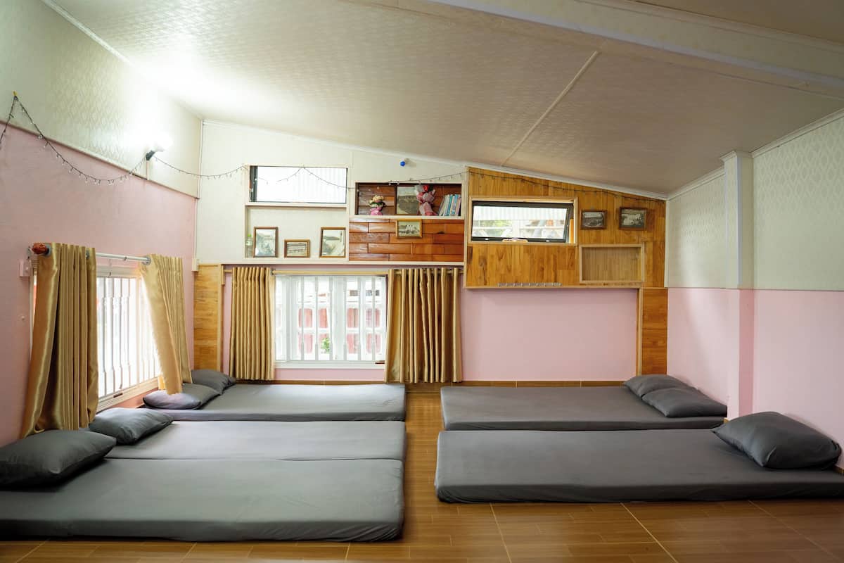 Quarto com quatro camas individuais, estantes de madeira e janela com cortinas.
