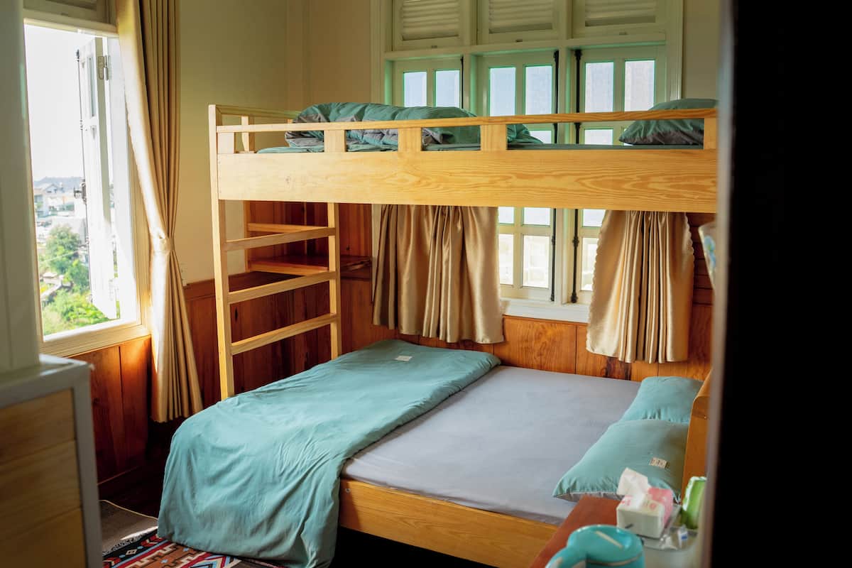 Quarto com beliche, janela, cortinas e escrivaninha com cadeira.