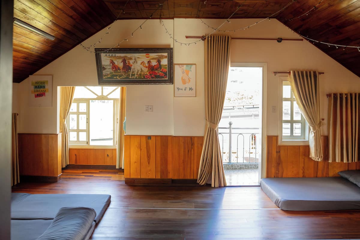 Quarto com piso de madeira, duas camas, um quadro e uma janela com cortinas.
