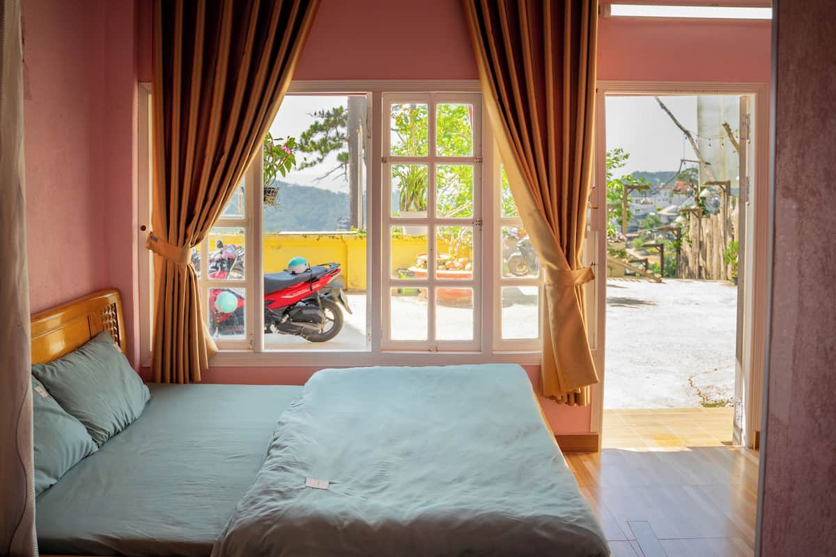 Quarto com cama, cortinas e janela com vista para uma motocicleta e edifícios.