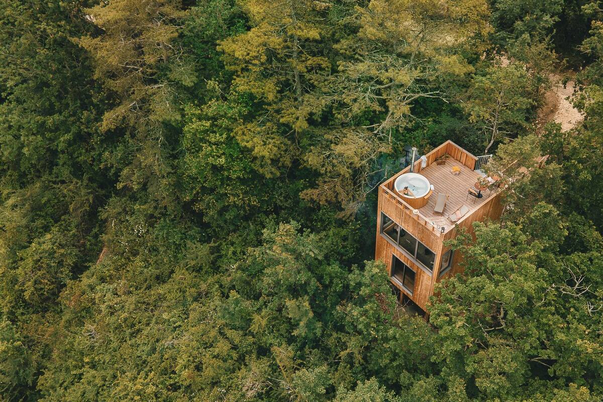 Uma cabana de madeira com banheira de hidromassagem, rodeada por uma floresta densa.
