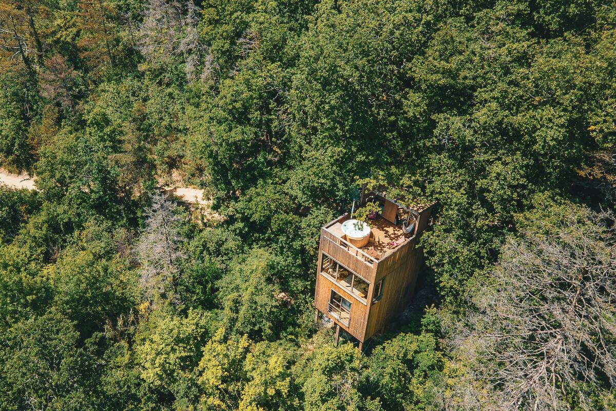 Uma cabana de madeira com hidromassagem no telhado, cercada por uma floresta densa.