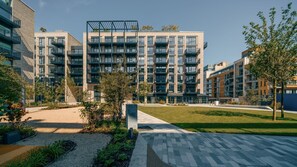 Um edifício moderno de vários andares com varandas, um pátio pavimentado e vegetação ao redor.