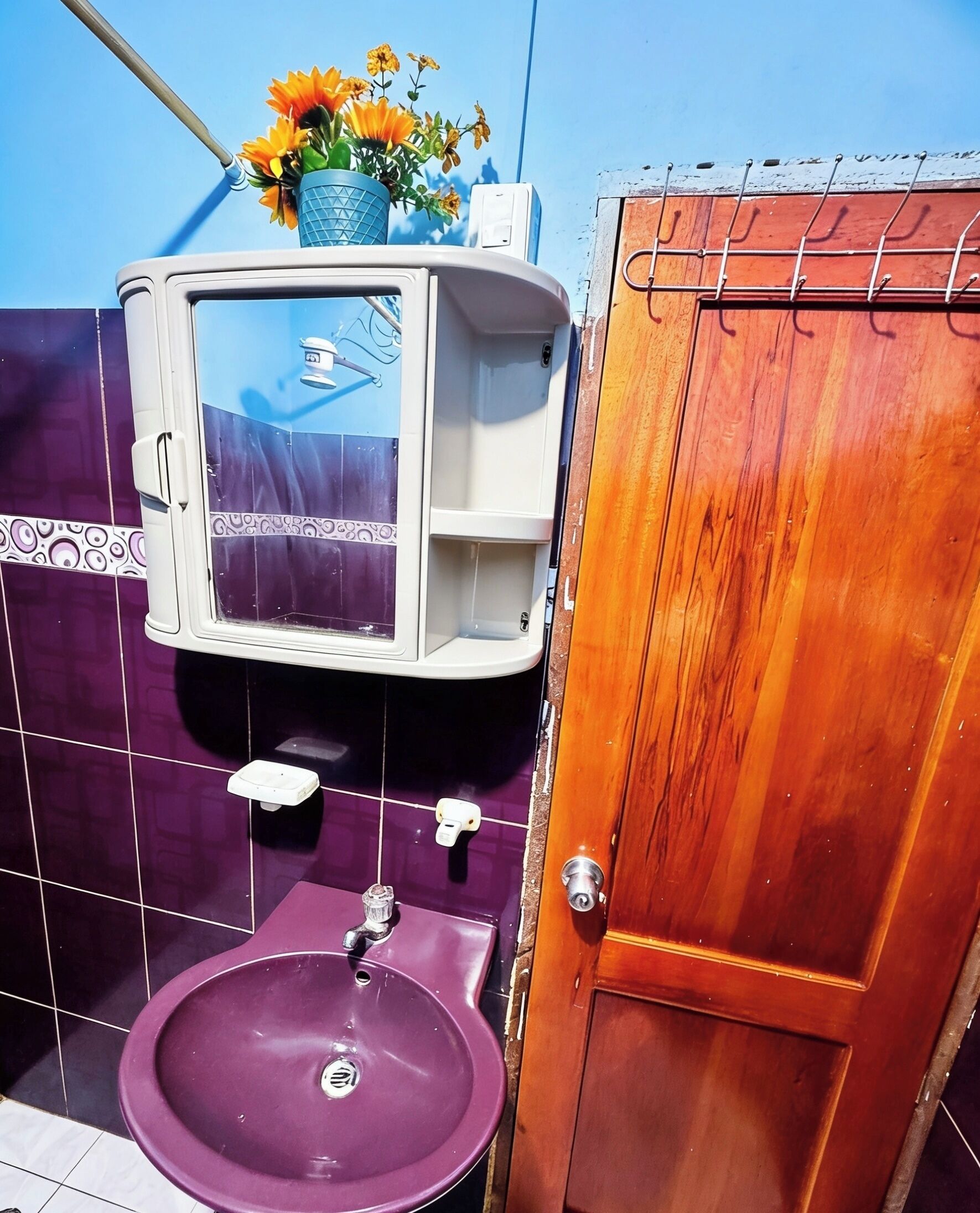 Um banheiro com uma pia roxa, um móvel de vaidade branco e uma porta de madeira.