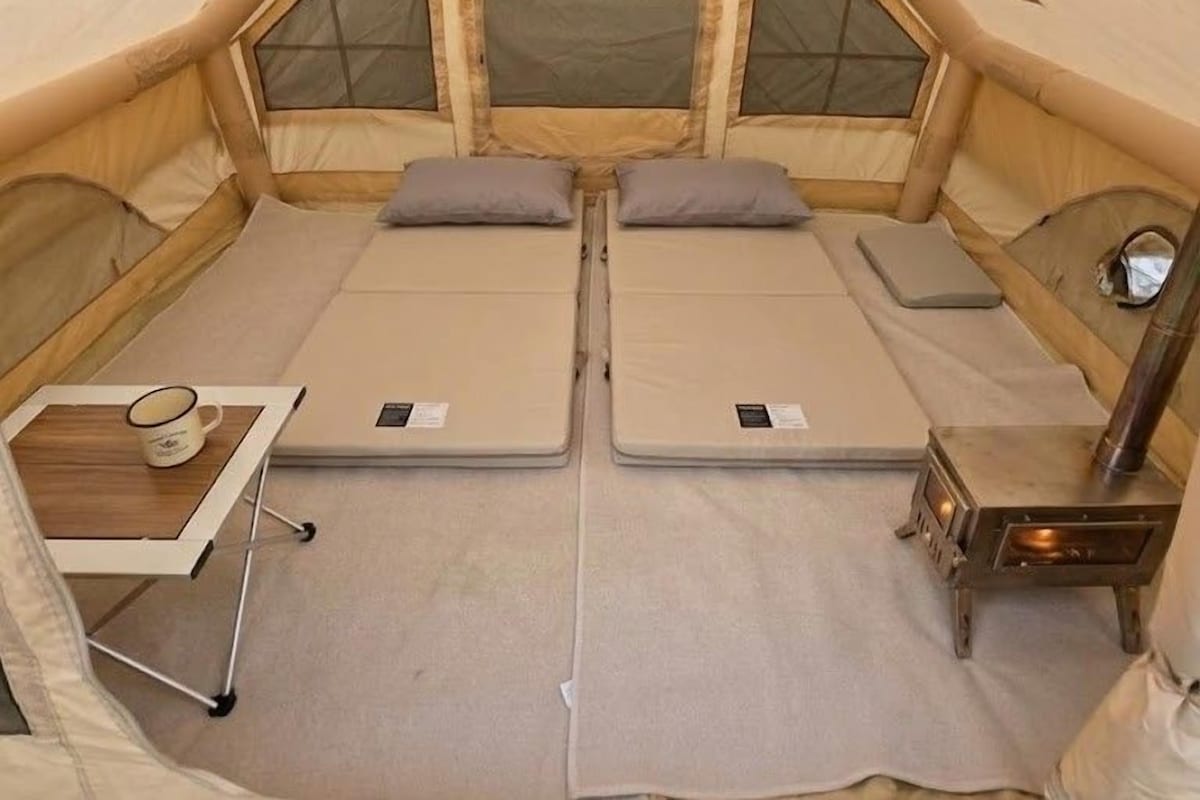 Tenda com duas camas, uma mesa com uma caneca e um aquecedor portátil.