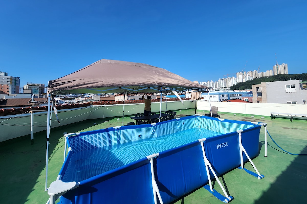 Piscina no terraço com toldo, rodeada por edifícios da cidade.