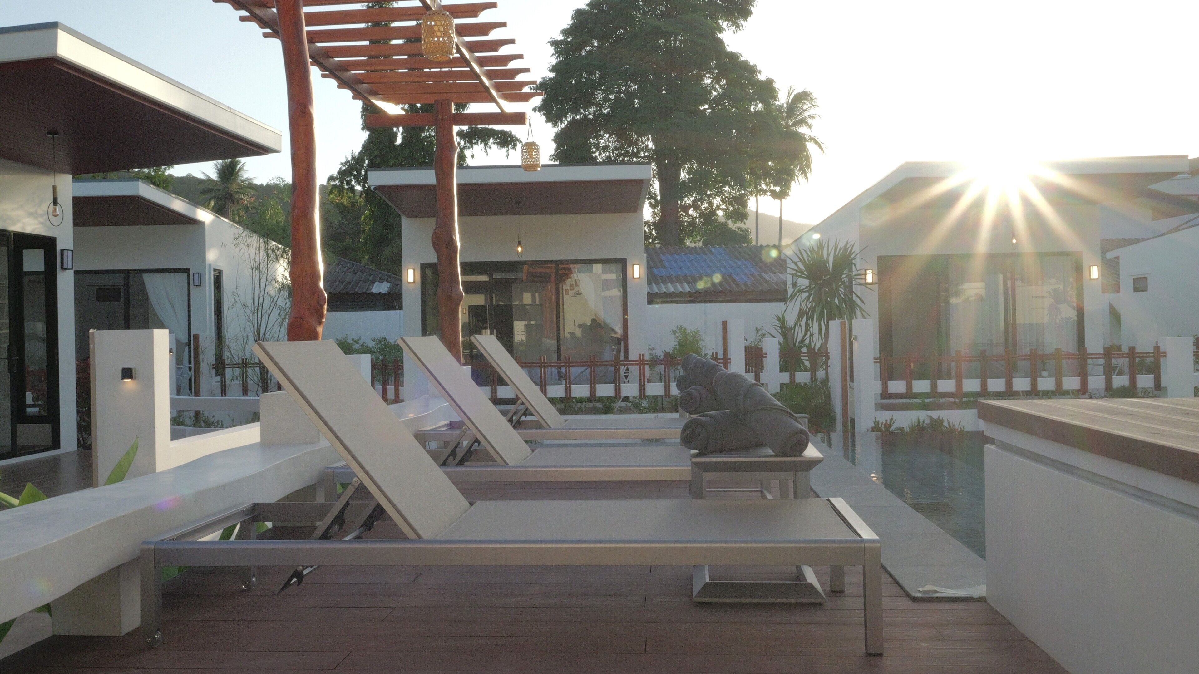 Uma área de estar ao ar livre moderna, com espreguiçadeiras, uma pérgula de madeira e uma piscina.
