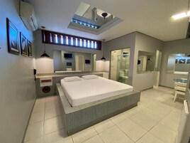 Quarto moderno com uma cama grande, claraboia e banheiro com chuveiro de vidro.