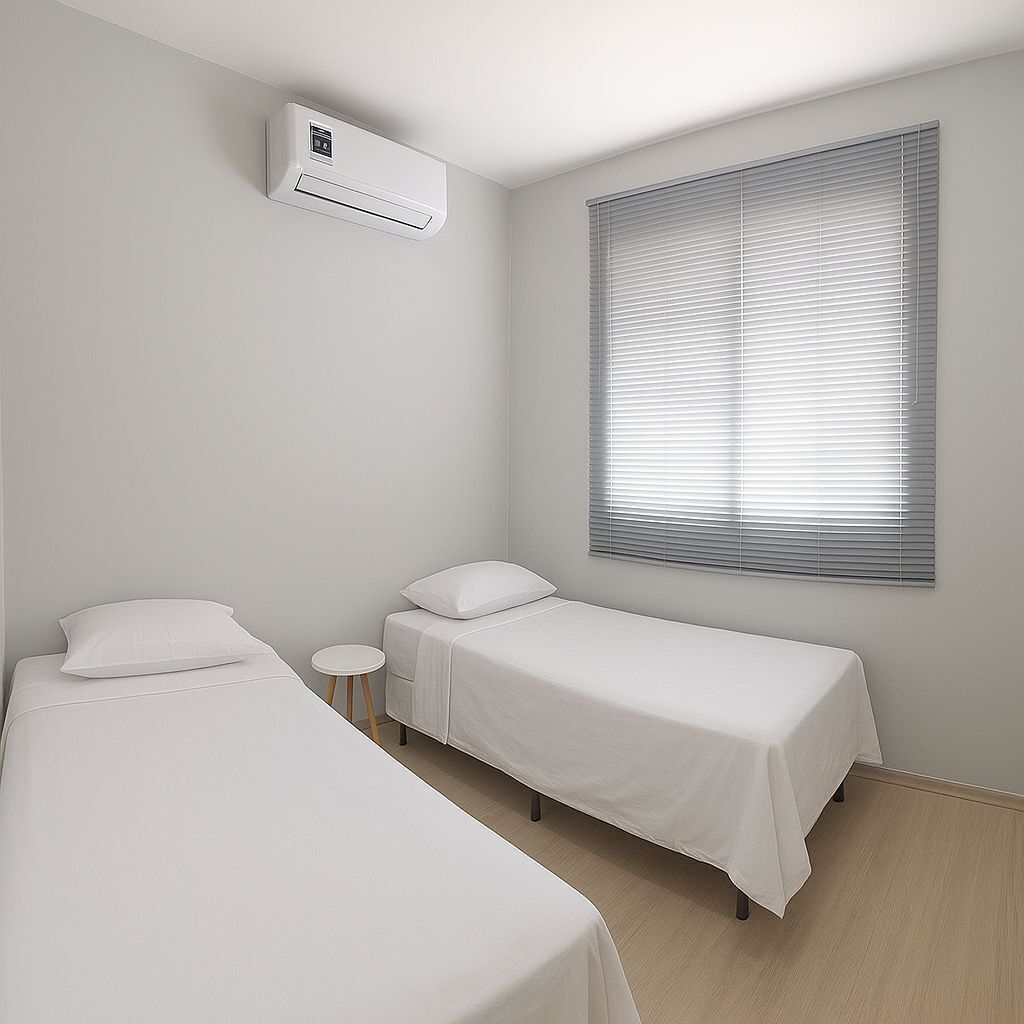 Quarto com duas camas de solteiro, uma mesinha redonda, ar-condicionado fixado na parede e uma janela com persianas.
