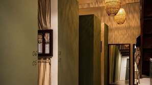 Um corredor com portas numeradas, um espelho e luminárias de vime suspensas.